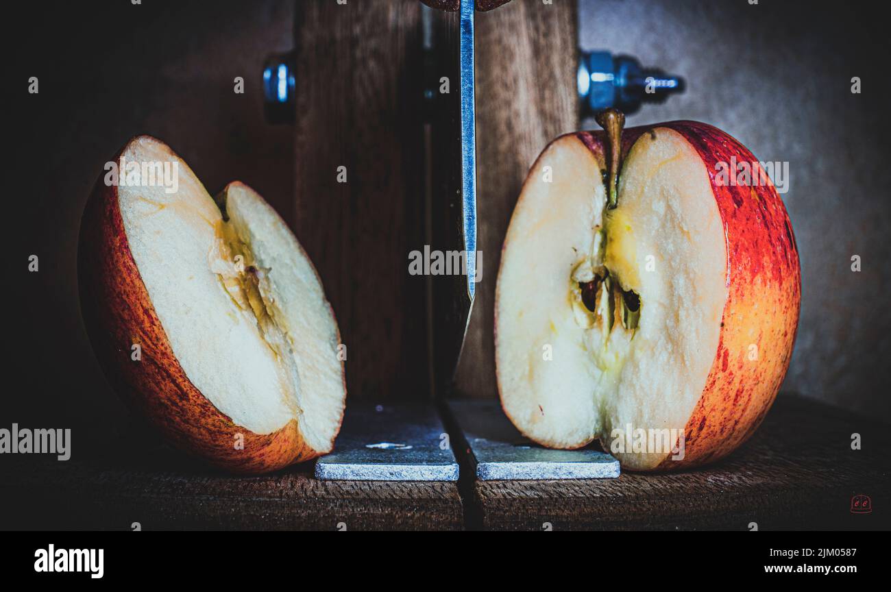 A closeup of a fresh red apple cut in half on a steel cutting machine ...