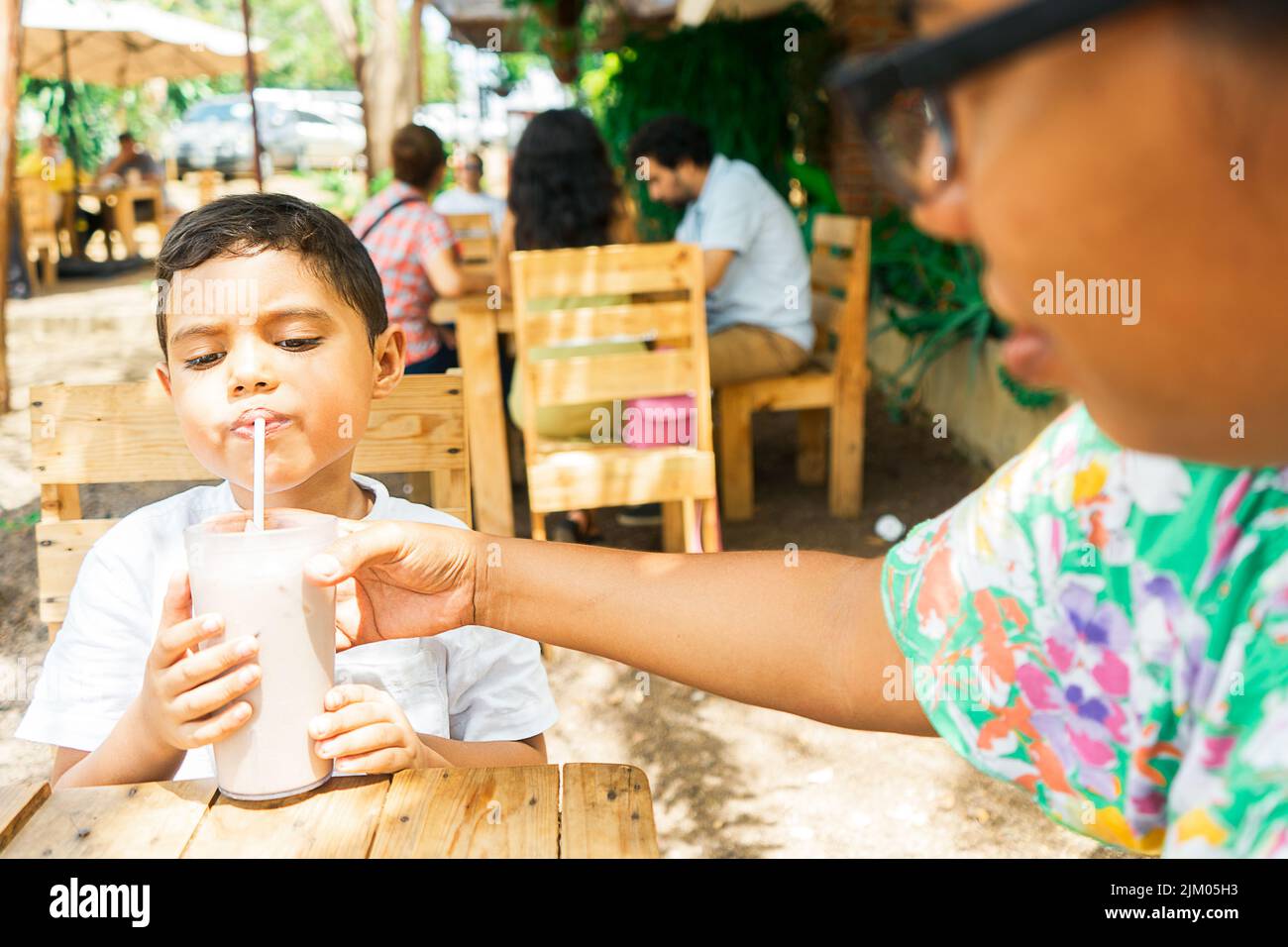 Latin mother giving her son a milkshake to drink in a country ...