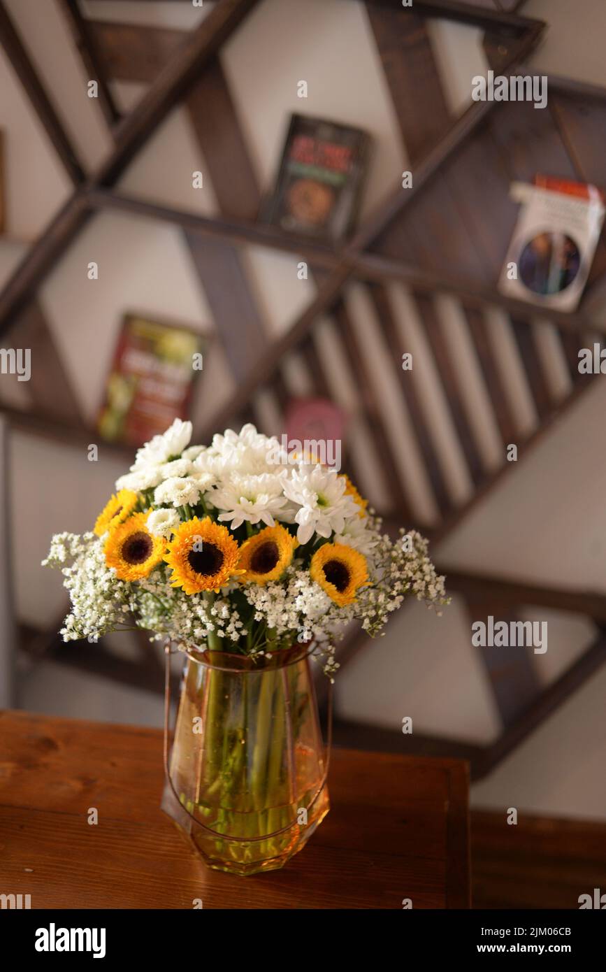 A vertical shot of a decorative vase with white flowers and sunflowers ...