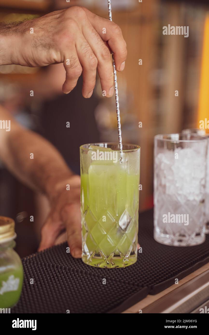 A vertical shot of a bartender mixing iced refreshing cocktails at a ...
