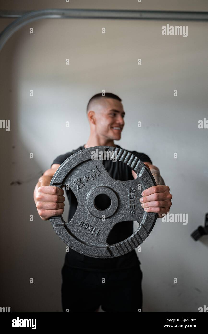 The vertical shot of an athlete man holding a rubber weight disc in his ...