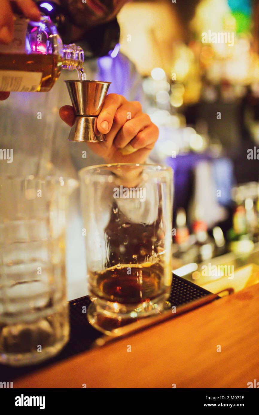 A vertical closeup of a glass being filled with an iced alcoholic drink ...