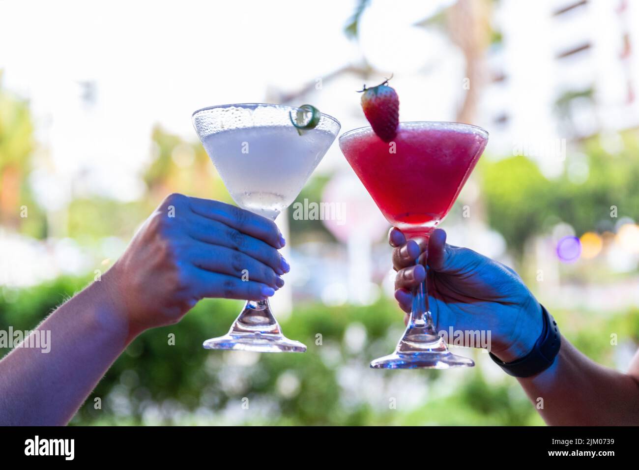A closeup of two hands cheering with a strawberry mocktail and a ...