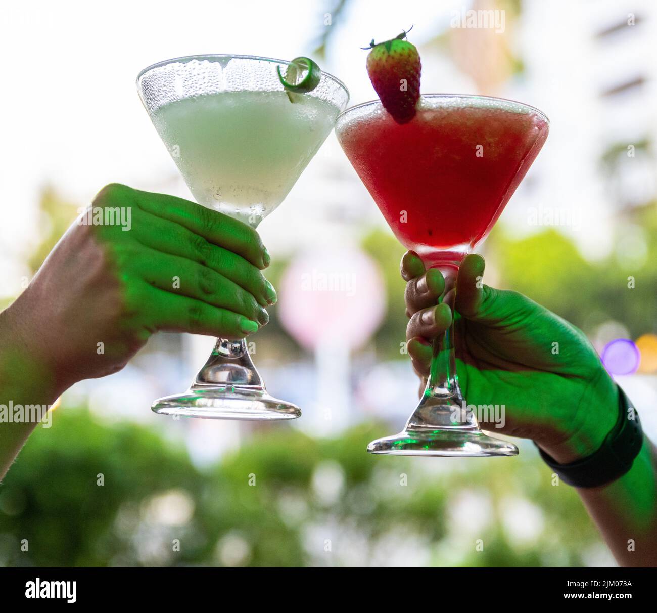 A closeup of two hands cheering with a strawberry mocktail and a ...