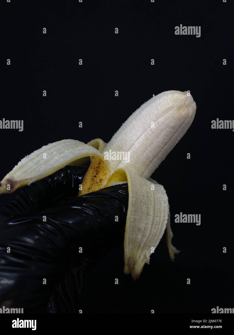 A vertical closeup of a pealed banana isolated on a black background ...