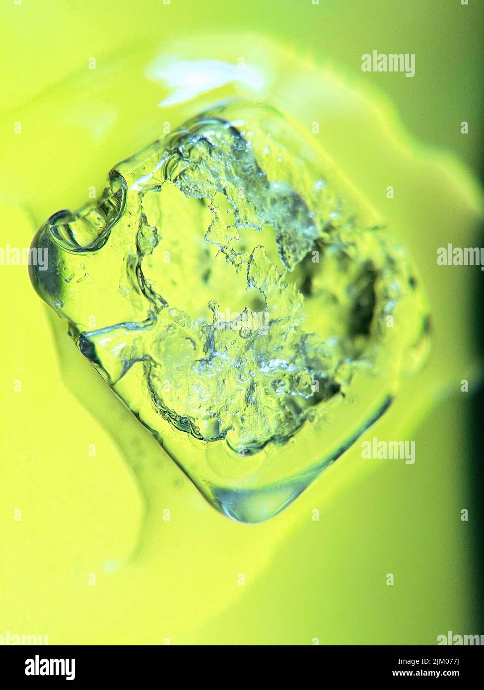 A vertical closeup of an ice cube melting on a green background Stock ...