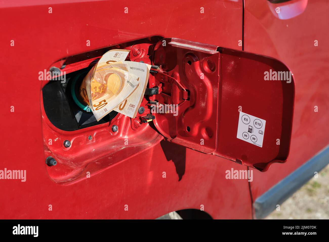 A bundle of fifty euro notes sticking out of a car's open fuel tank. A ...