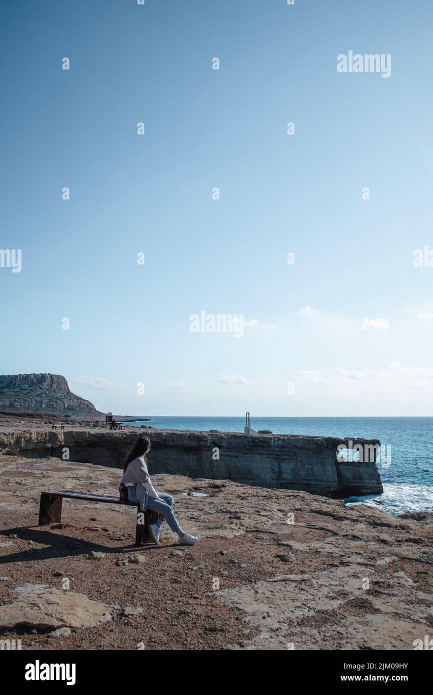 Young woman is sitting on a bench and looking at sea caves near cape ...