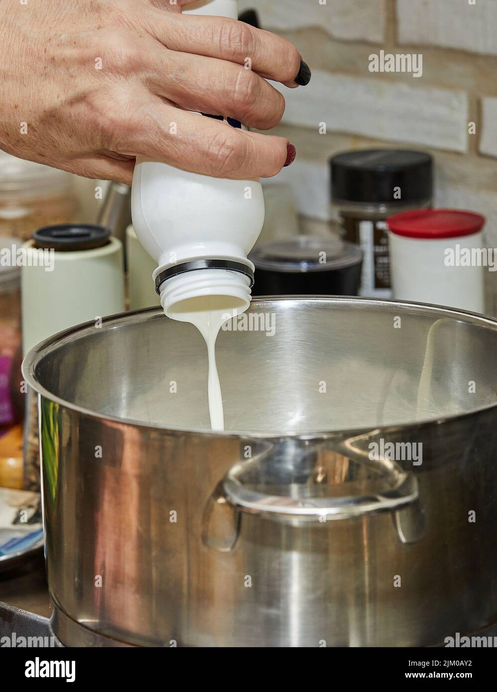 Chef pours cream from bottle into pan on gas stove Stock Photo - Alamy