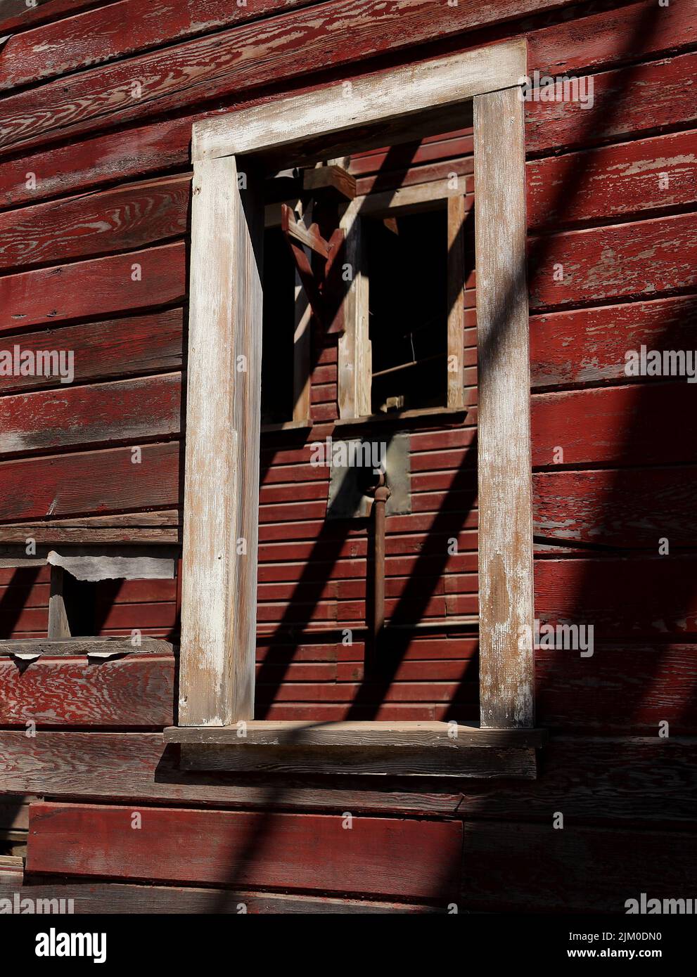 A vertical shot of an abandoned red house exterior with a broken window ...