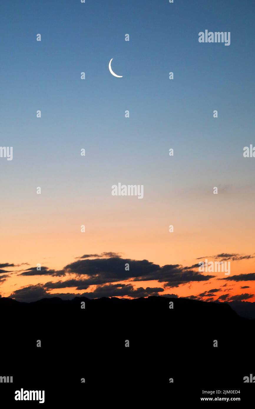 narrow band of the moon with the colorful setting sun and black outline ...