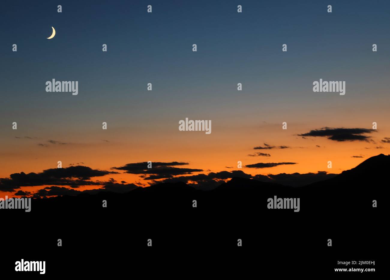 narrow band of the moon with the colorful setting sun and black outline ...