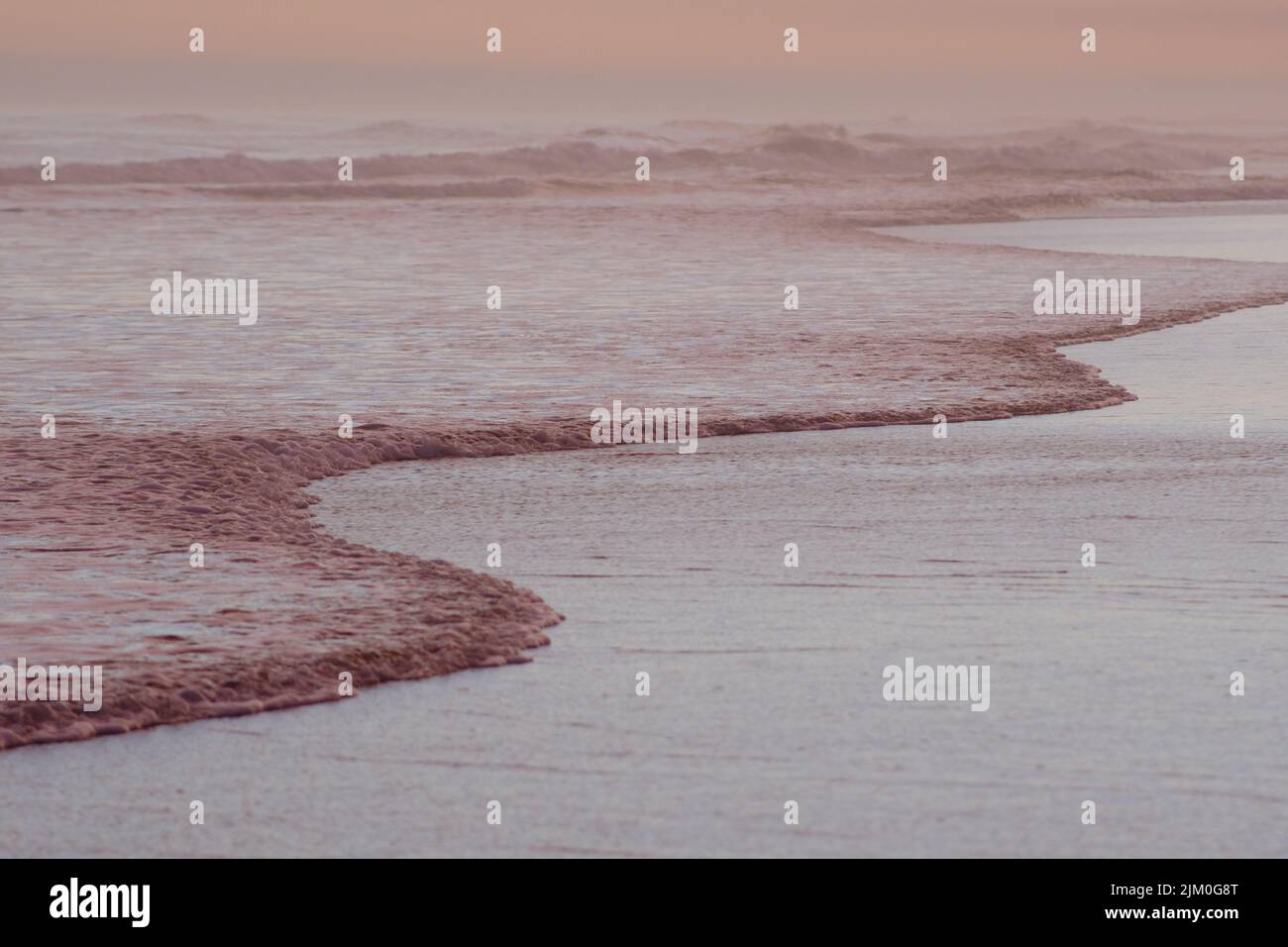 A beautiful sandy beach with calm water over a background of pinkish ...