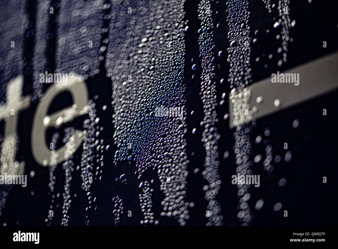 A closeup of small water drops on a surface of black glass with letters ...