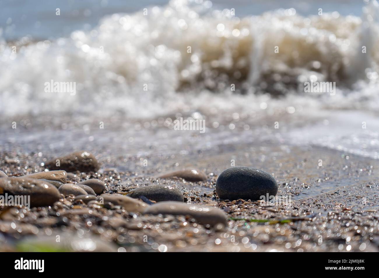 A selective focus shot of pebbles on the beach and a wave on blurred ...