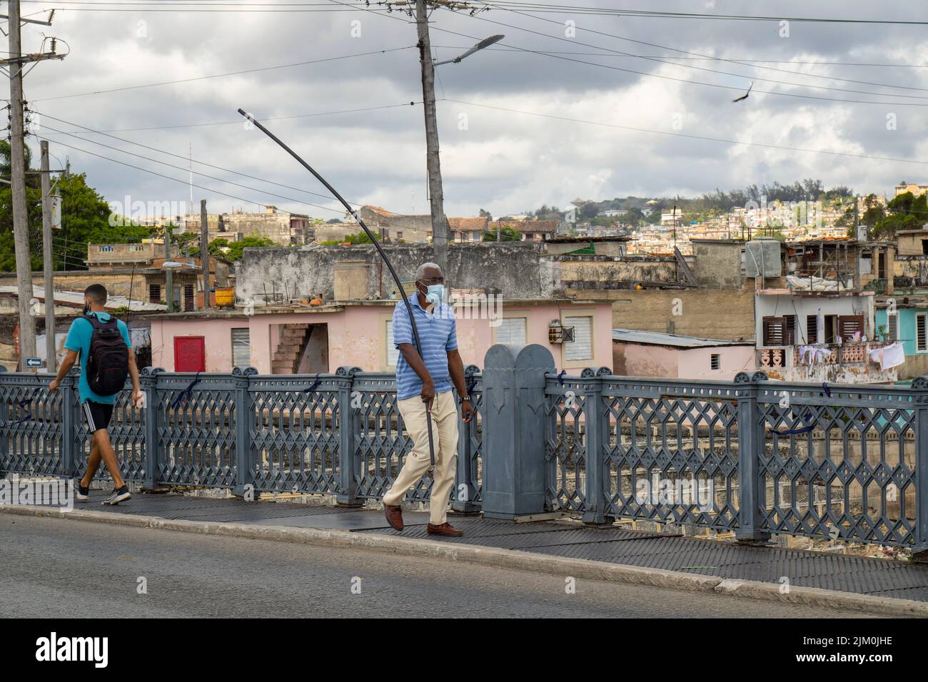 An elderly person carrying a water pipe across a bridge in Matanzas ...