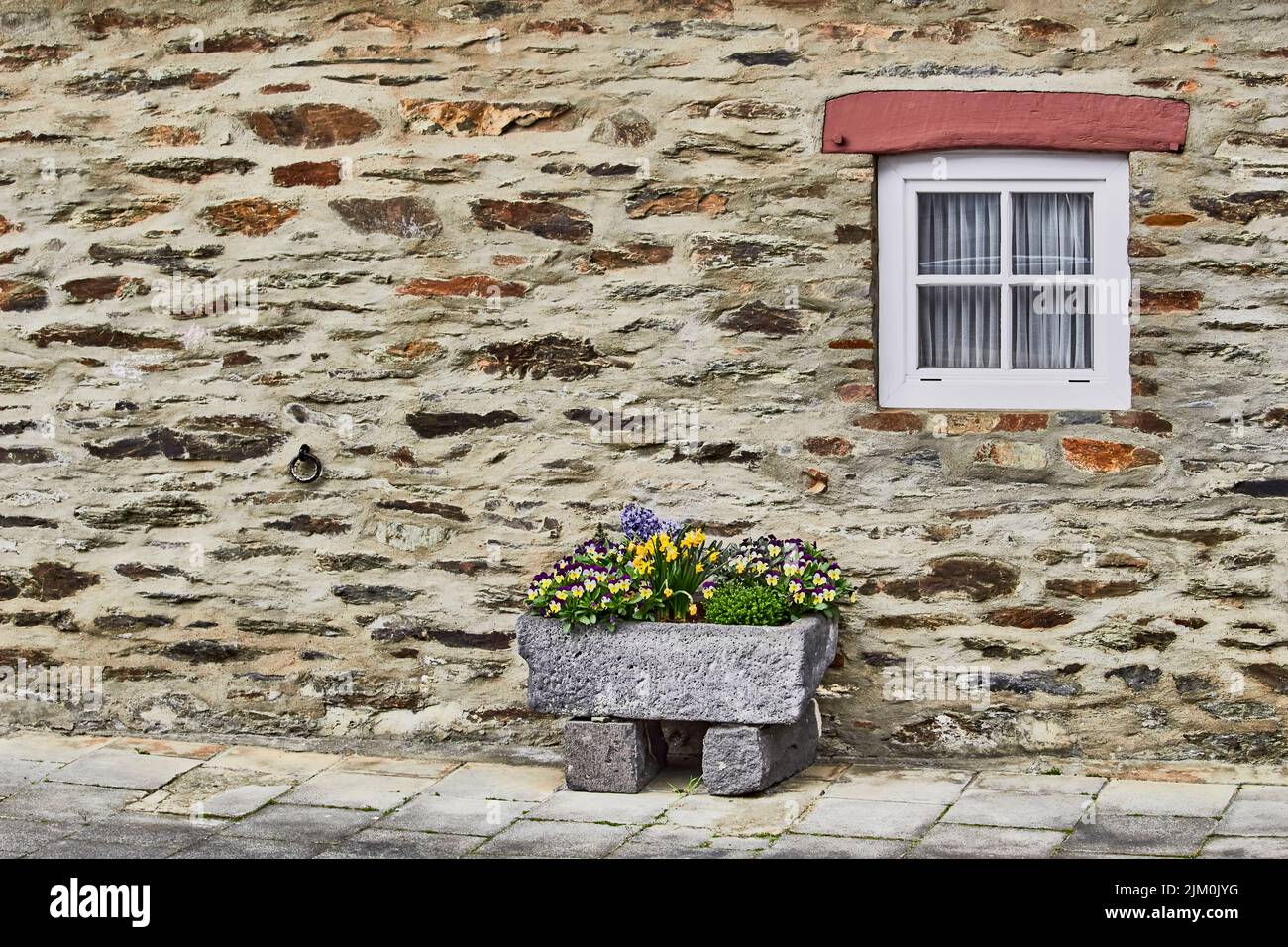A beautiful exterior old stone wall building with a window and plants ...