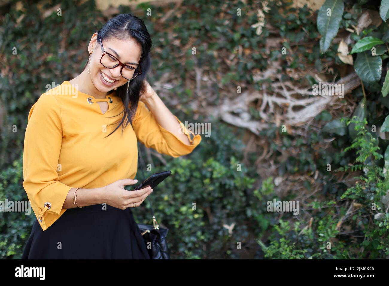 Young woman using and looking phone smiling with leaves background at ...