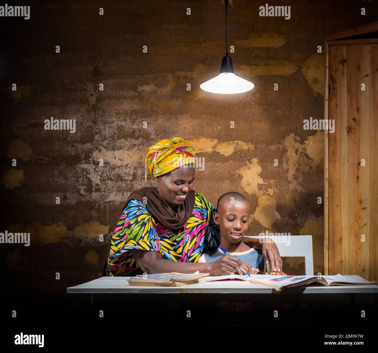 A Rwandan mother helping her child with homework at home with a light ...