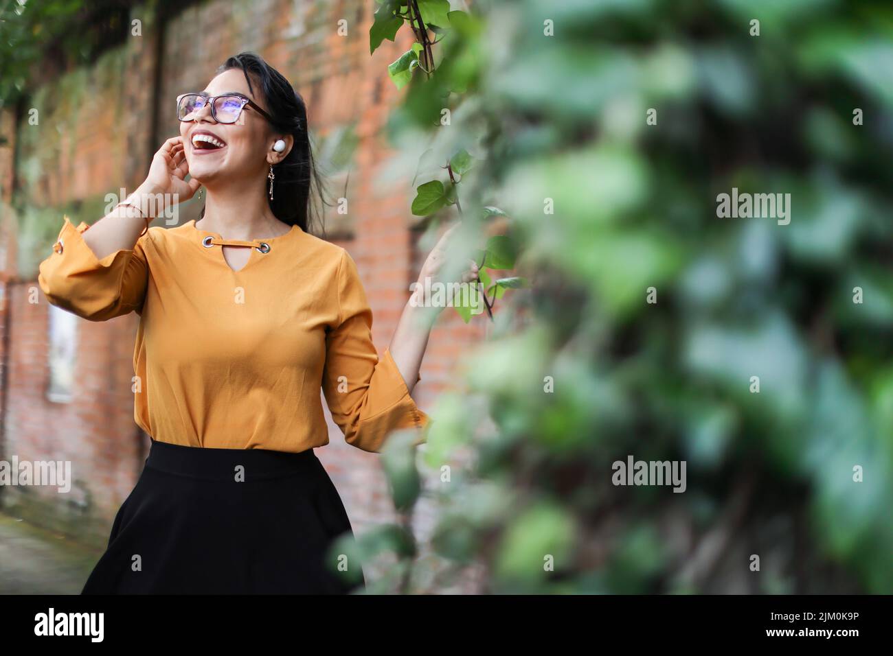 Young Latin American woman wearing eyeglasses and earbuds looking up ...