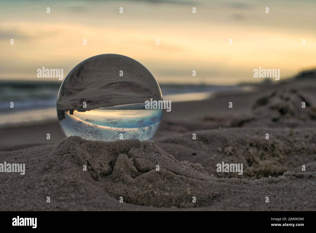 A closeup shot of a glass ball on sand reflecting the beautiful view of ...