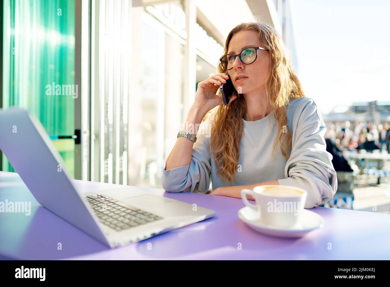 Beautiful young woman with laptop talking on the phone at outdoor cafe ...