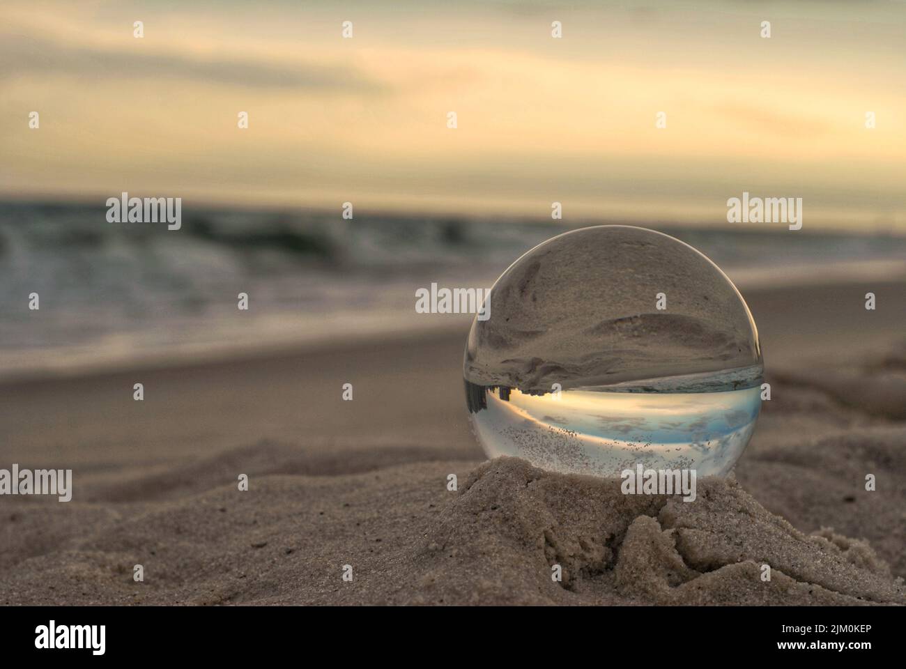 A closeup shot of a glass ball on sand reflecting the beautiful view of ...