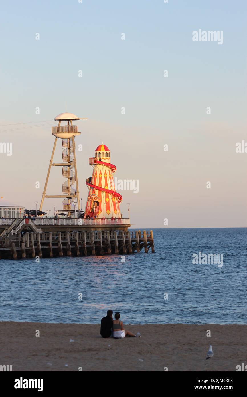 A view of couple sitting on beach in background of Helter skelter on ...