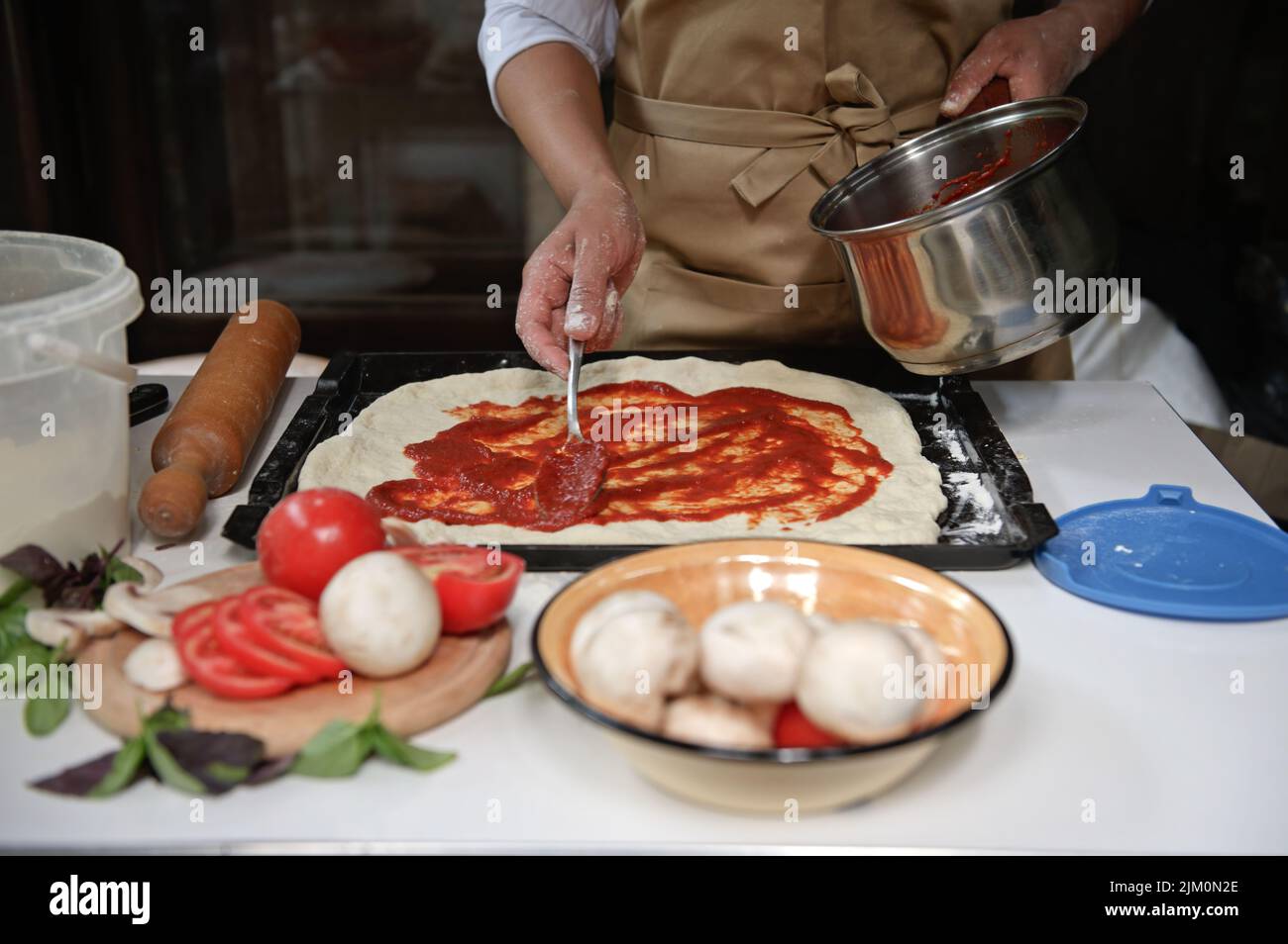 Front view housewife in beige chef apron spreads freshly made tomato ...