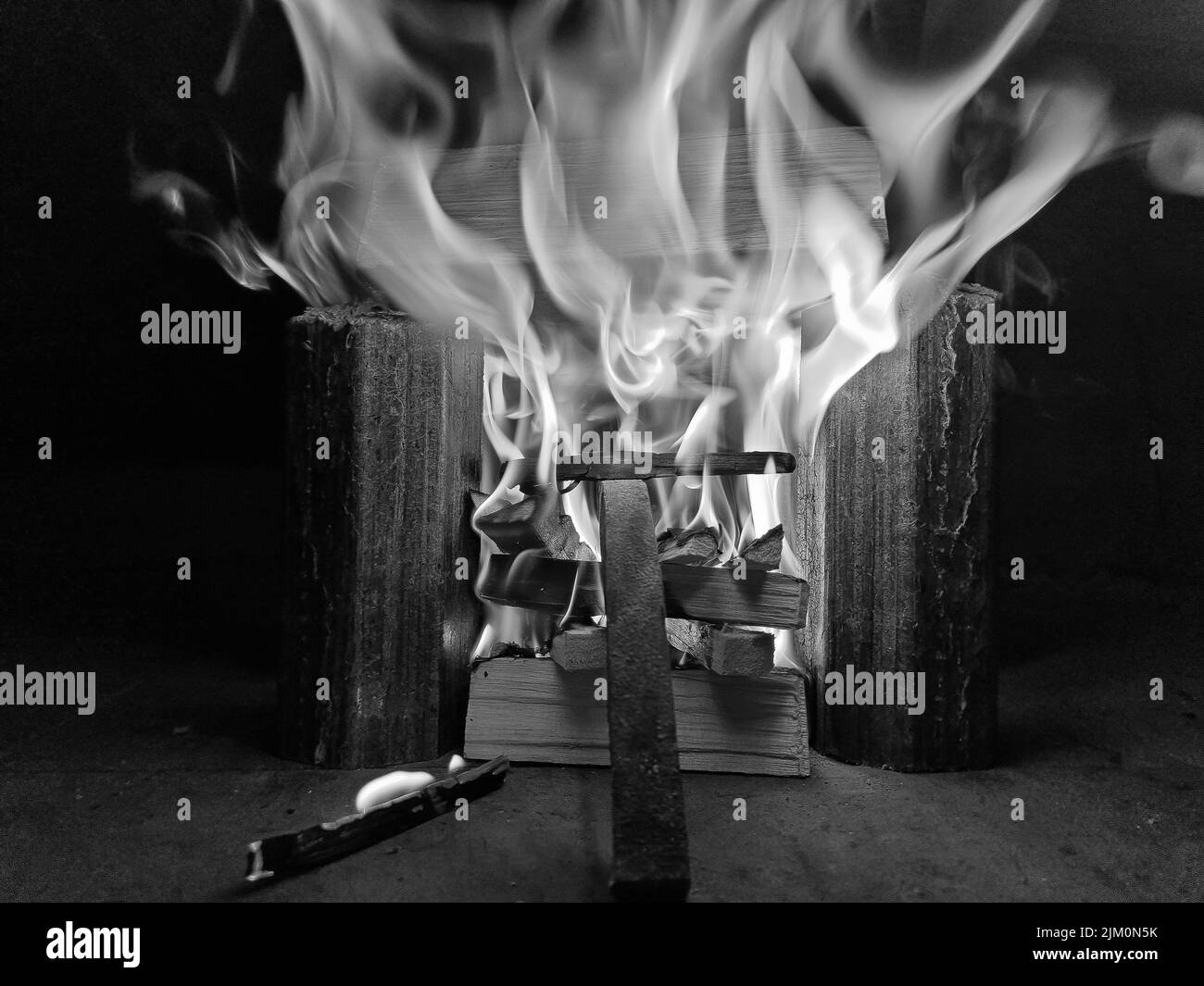 A grayscale shot of pieces of wood being burnt with smoke and flames ...