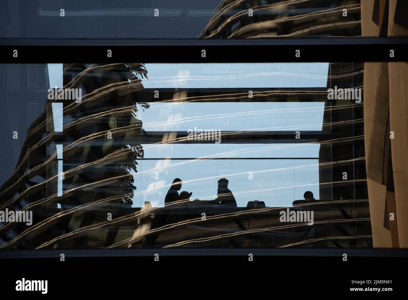 The silhouette of people sitting at a cafe reflected on a glass window ...