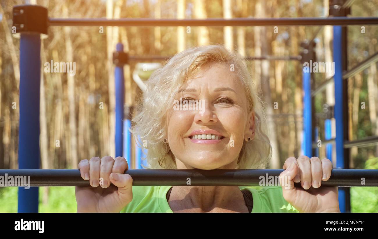 Mature woman does pull-ups smiling on sports ground closeup Stock Photo ...