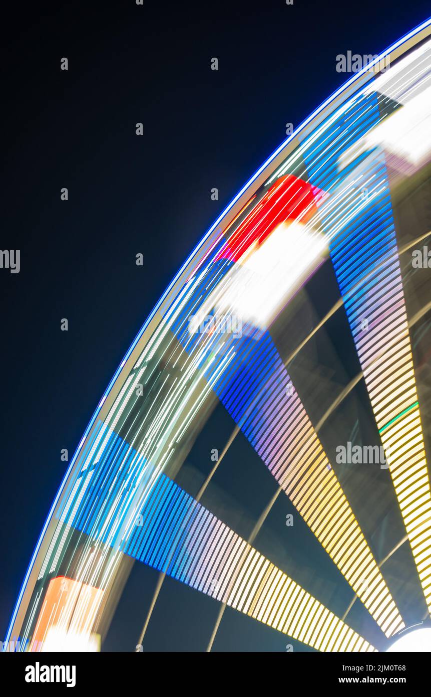 A vertical shot of the edge of a colorful Ferris wheel moving in the ...