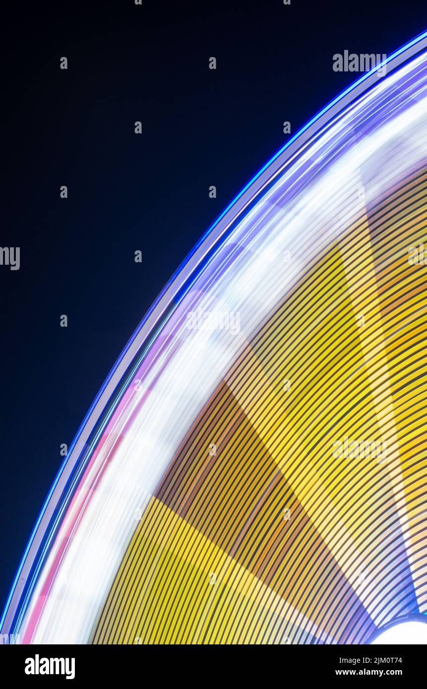 A vertical shot of the edge of a blurry Ferris wheel ride at night with ...