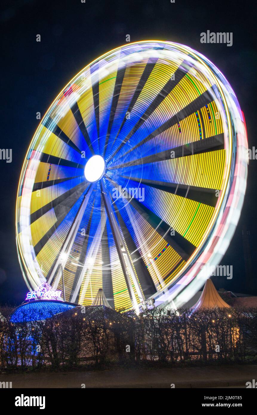 A vertical shot of a Ferris wheel with bright blurry neon lights ...