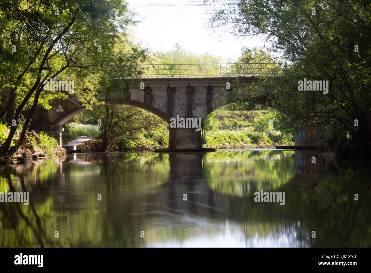 A scenic view of an arcade bridge surrounded by greenery reflecting on ...