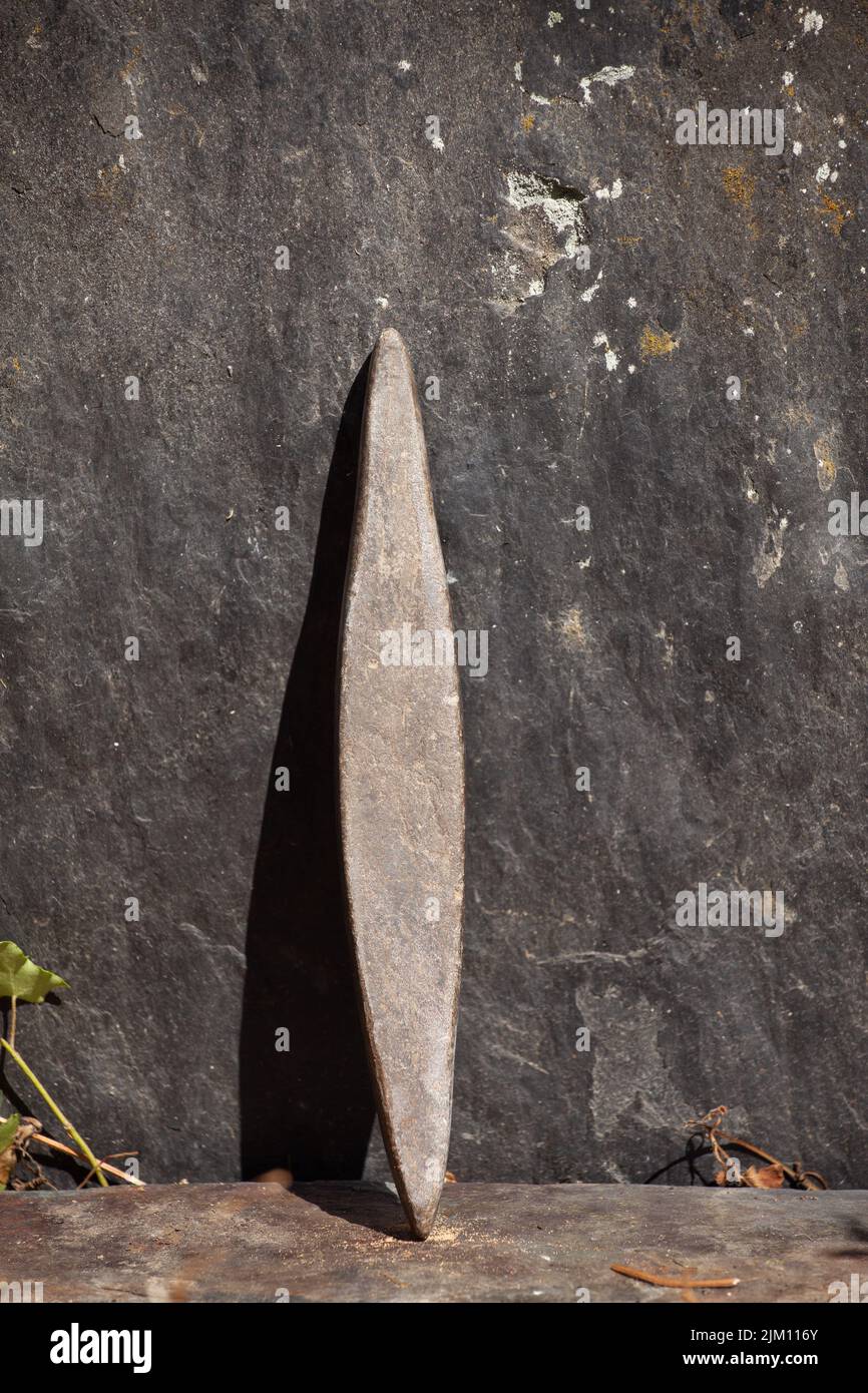 An old, worn whetstone sits against a large piece of shale. It has an ...