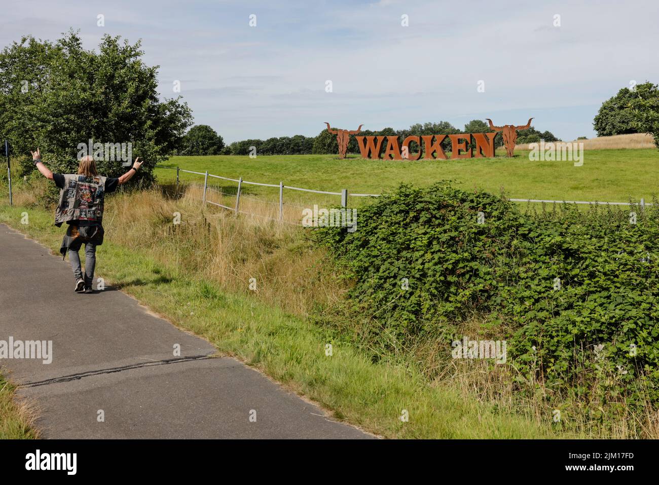 Wacken, Germany. 04th Aug, 2022. A metal fan walks past a sign of WOA ...