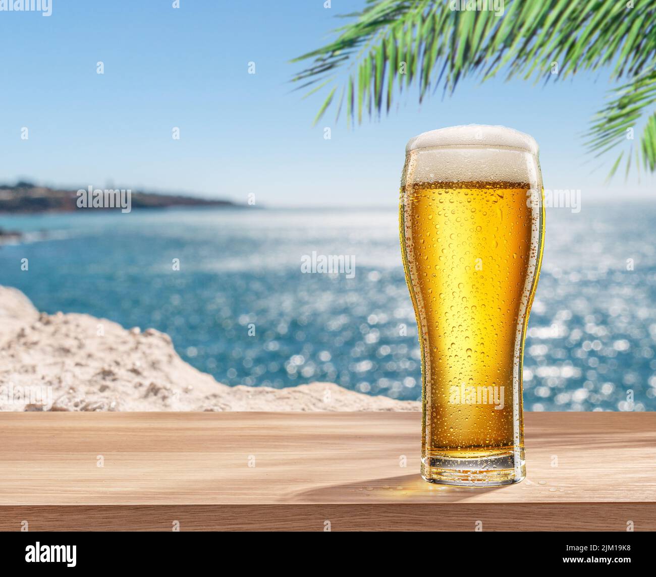 Glass of chilled beer on table and blurred sparkling sea at the ...