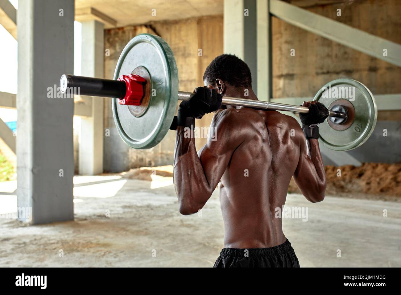Athletic black young man lifting a heavy-weight barbell in outdoor gym ...