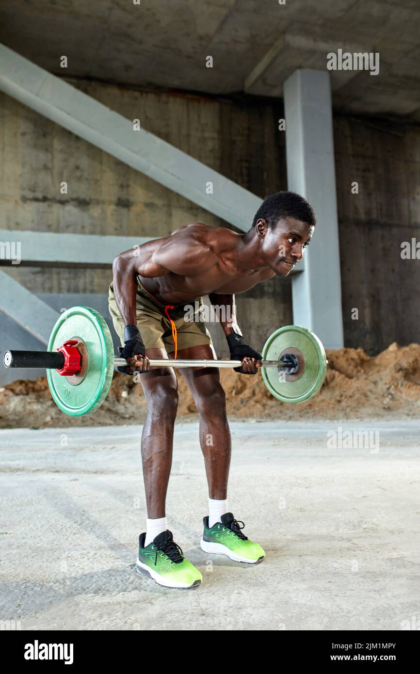 Athletic black young man lifting a heavy-weight barbell in outdoor gym ...