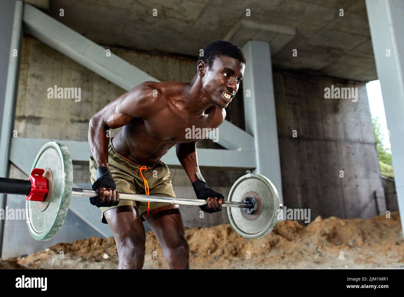 Athletic black young man lifting a heavy-weight barbell in outdoor gym ...