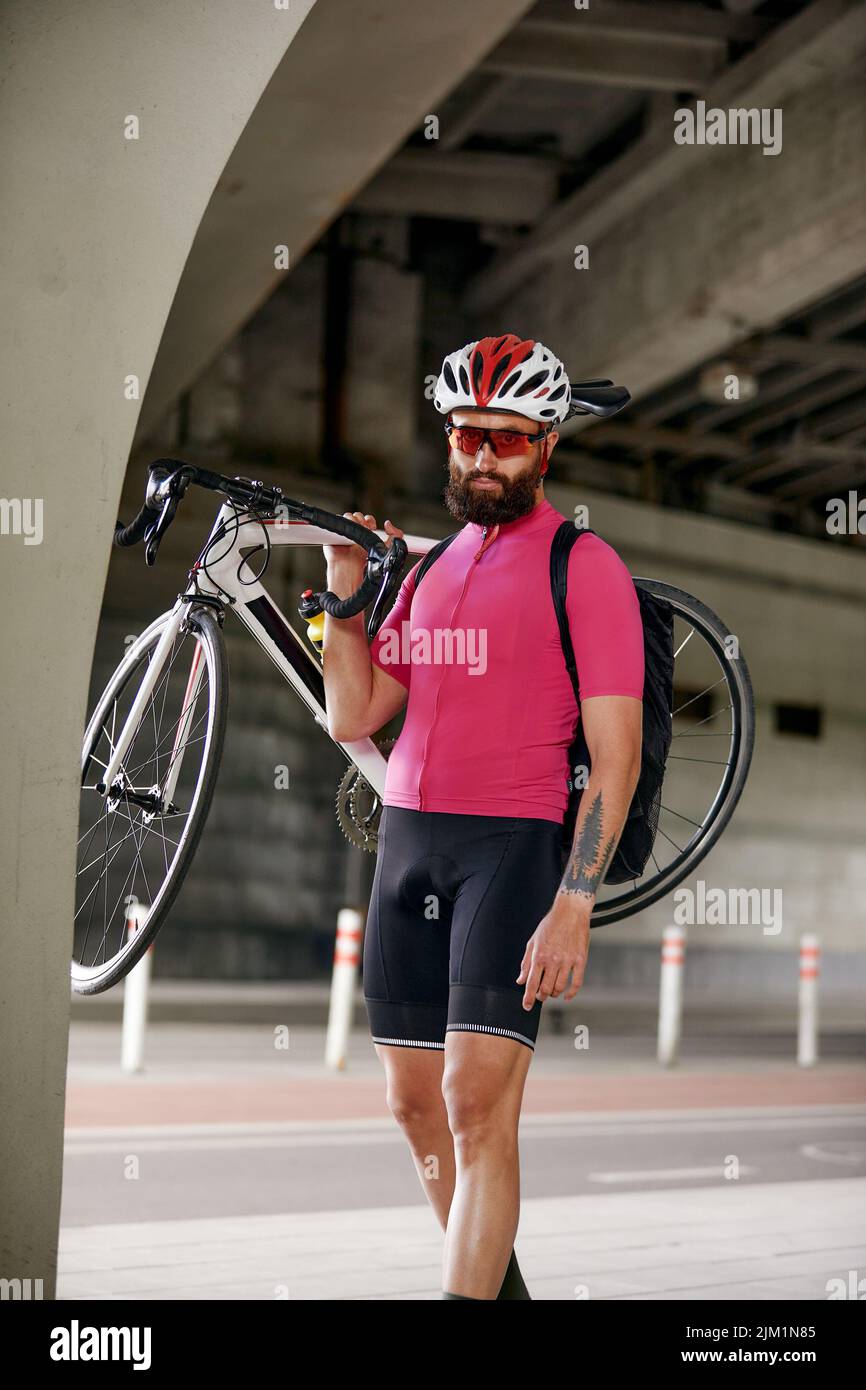 Portrait of a cyclist standing under a bridge with a bicycle in his ...