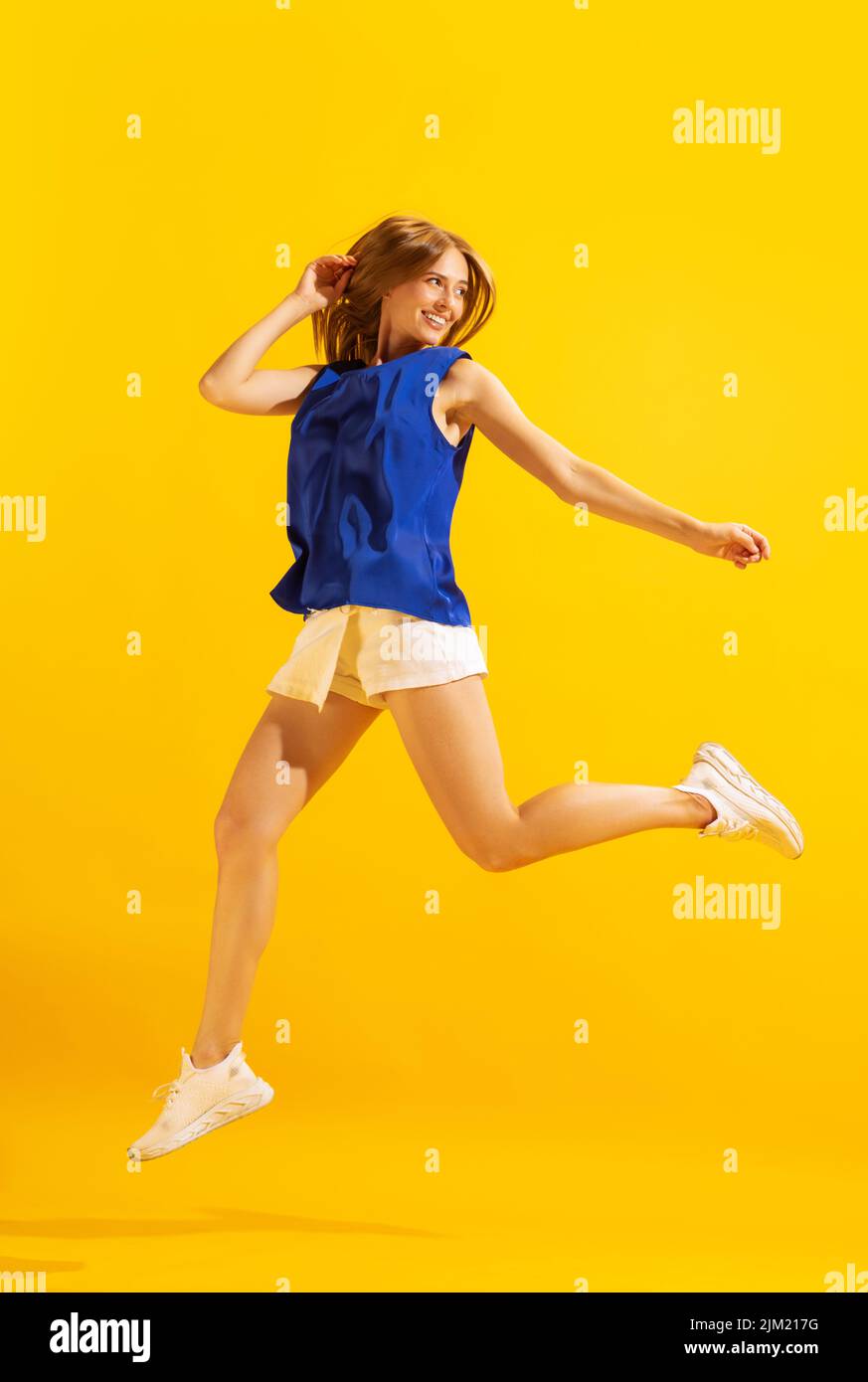 Happy young girl, student jumping isolated on bright yellow background ...