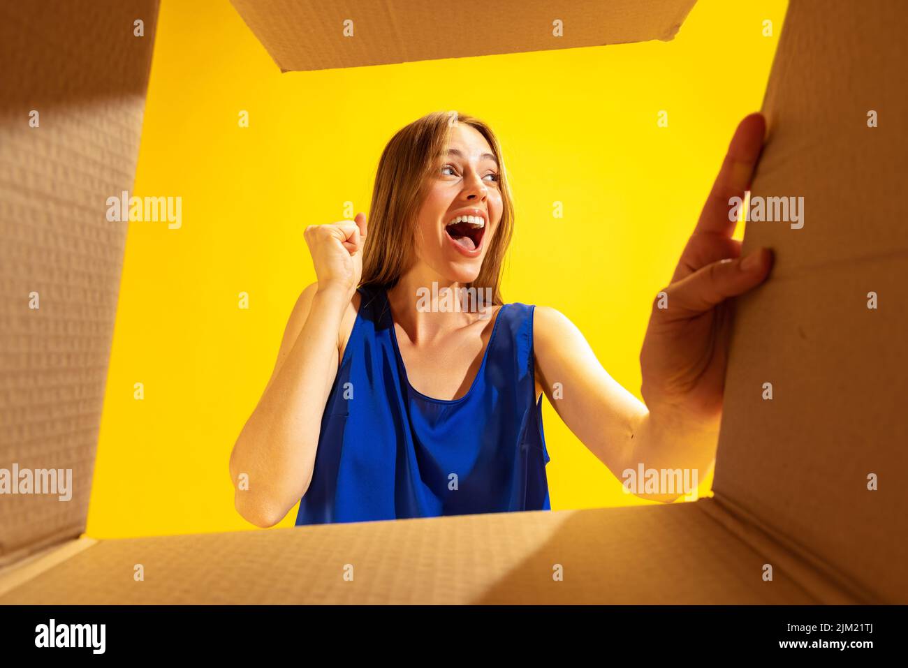 Astonished girl unpacking, opening carton box and looking inside ...