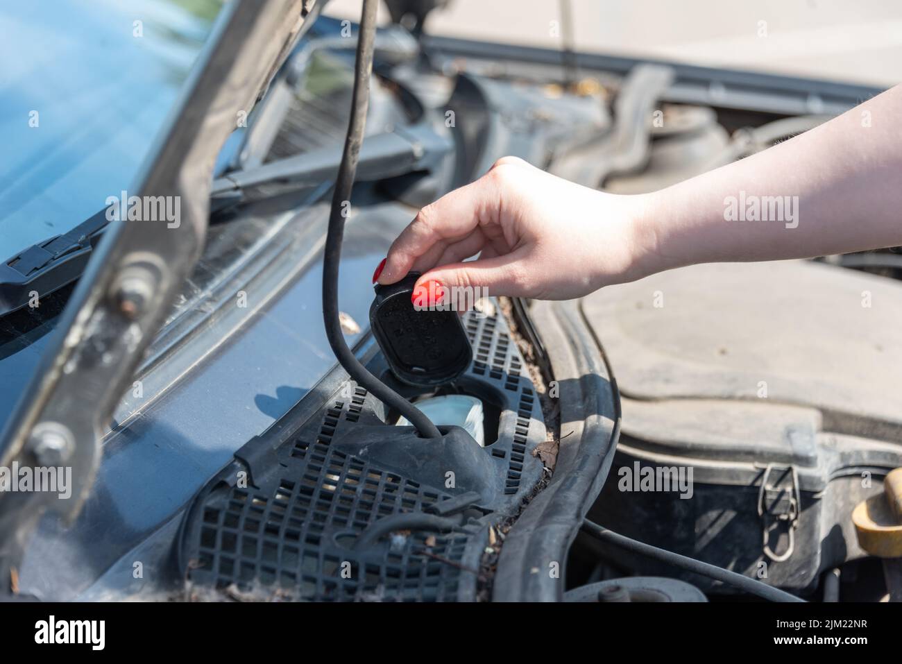 A woman's hand opens the lid of the tank to fill the car's windshield ...