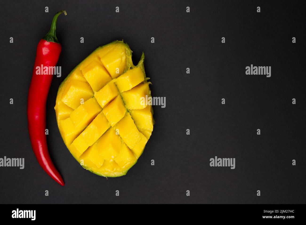 Cutted half of mango and whole chili pepper on dark grey background ...