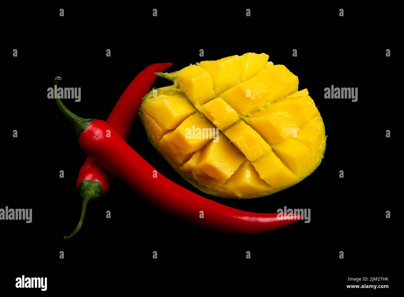Cutted mango and two whole chili peppers on black background ...