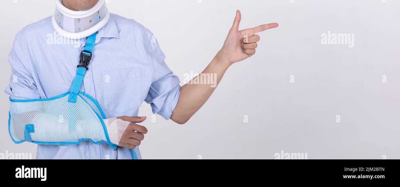 Portrait of smiling Asian man with broken arm and neck pointing finger ...