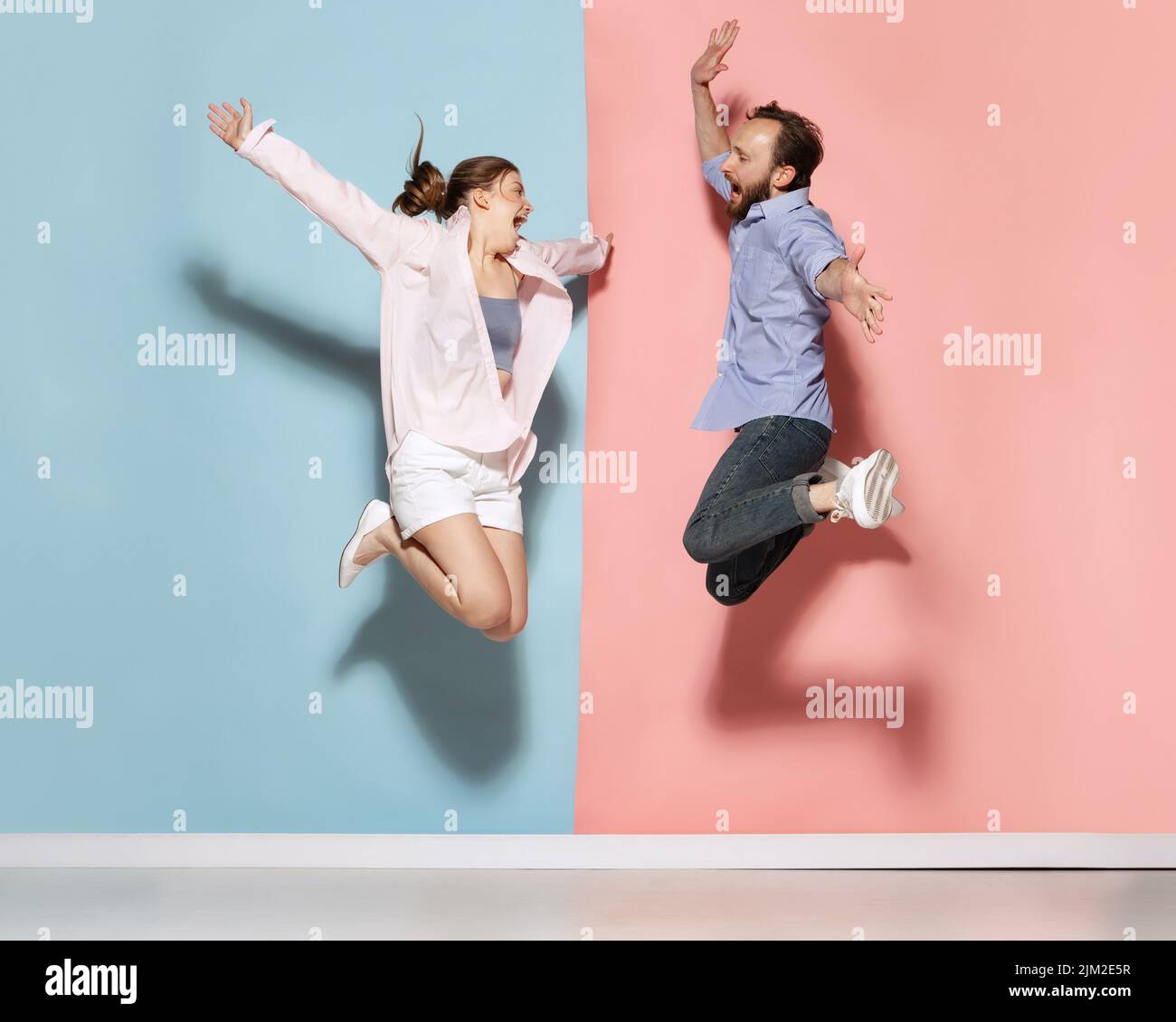Astonished man and woman running, jumping isolated over blue and pink ...